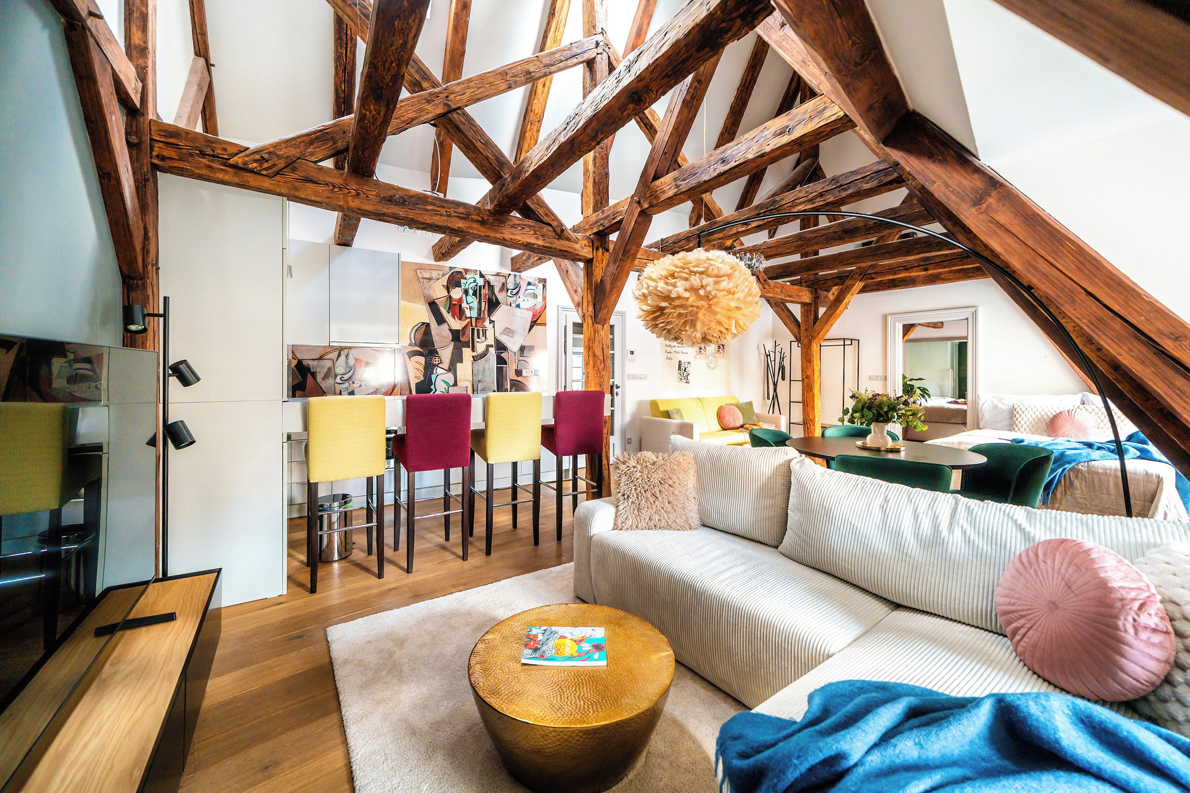 Um espaço de estar estilo loft com vigas de madeira aparentes, um sofá, uma mesa de centro e uma área de jantar com cadeiras.