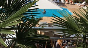 Área de piscina com espreguiçadeiras e uma pessoa nadando.