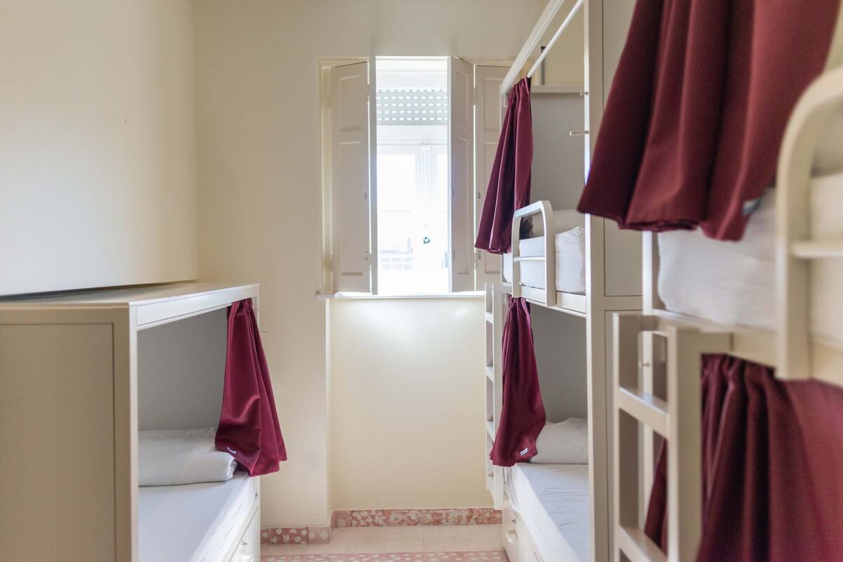 Um corredor estreito com beliches em ambos os lados, cada um com uma cortina vermelha.