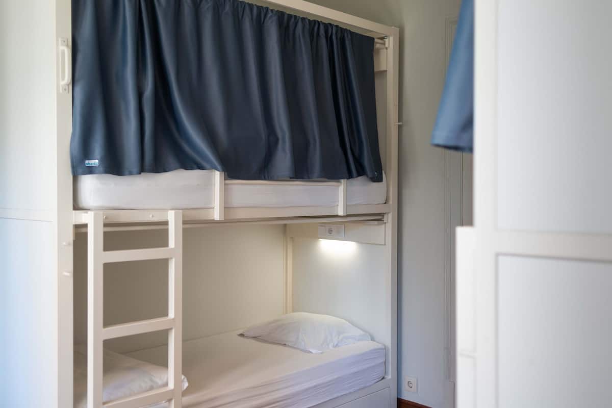 Uma cama beliche com estrutura branca e cortina escura.