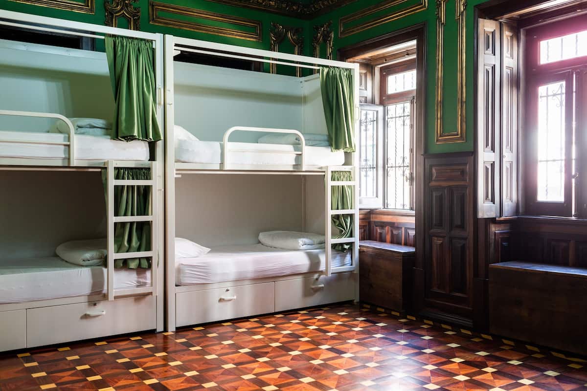 Quarto com duas beliches, piso de madeira e janela com cortinas.