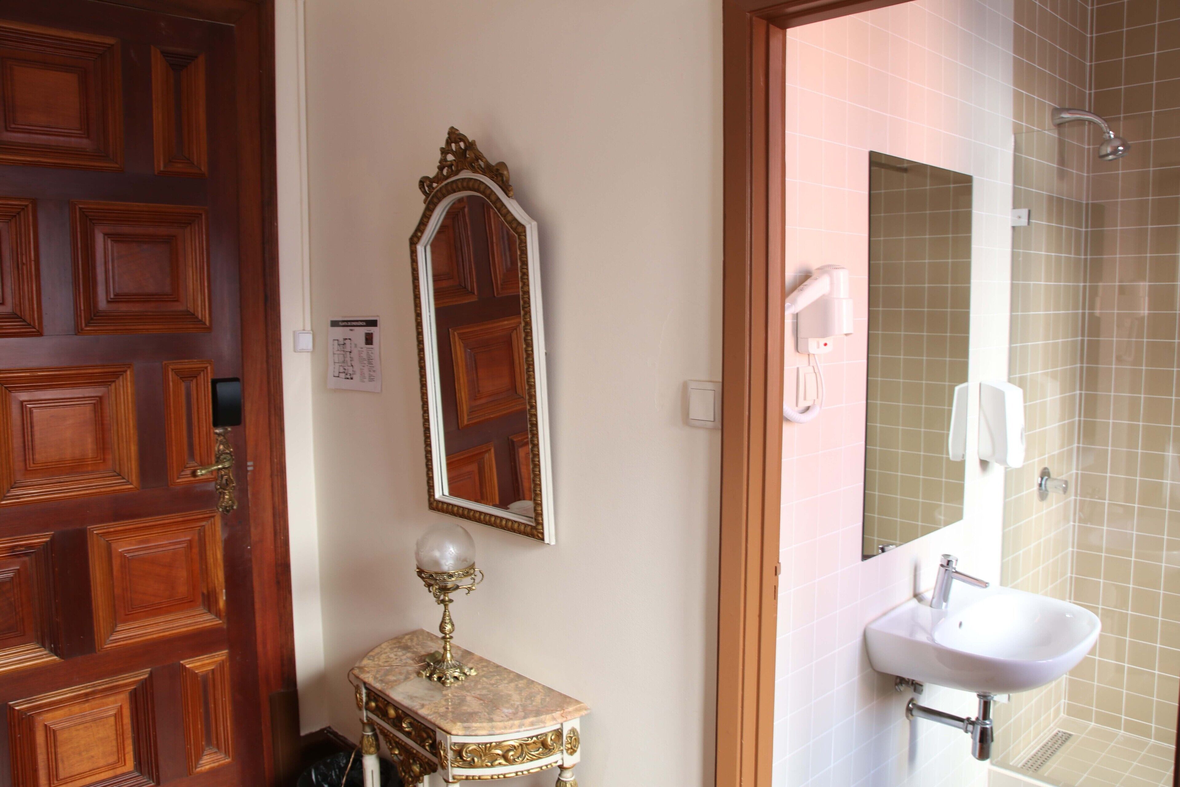 Um banheiro com porta de madeira, toucador de mármore com espelho, pia e chuveiro.