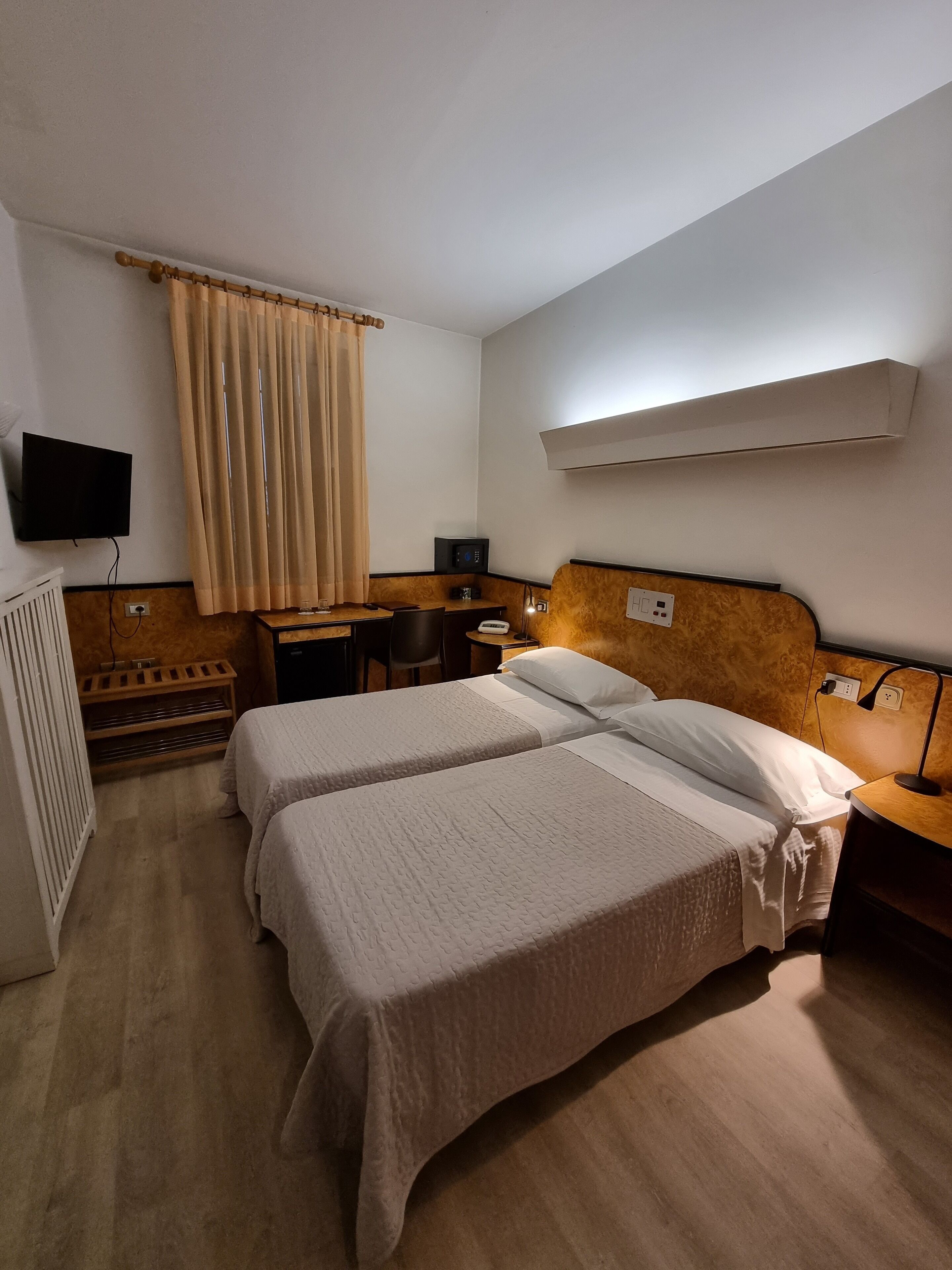 Quarto de hotel com duas camas, uma escrivaninha, uma cadeira, uma televisão e um aquecedor.