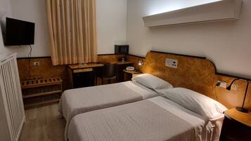 Quarto de hotel com duas camas, uma escrivaninha, uma cadeira, uma televisão e um aquecedor.