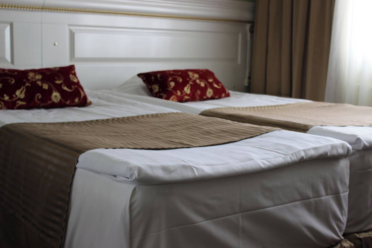 Quarto de hotel com duas camas, cada uma com colcha branca e manta marrom.
