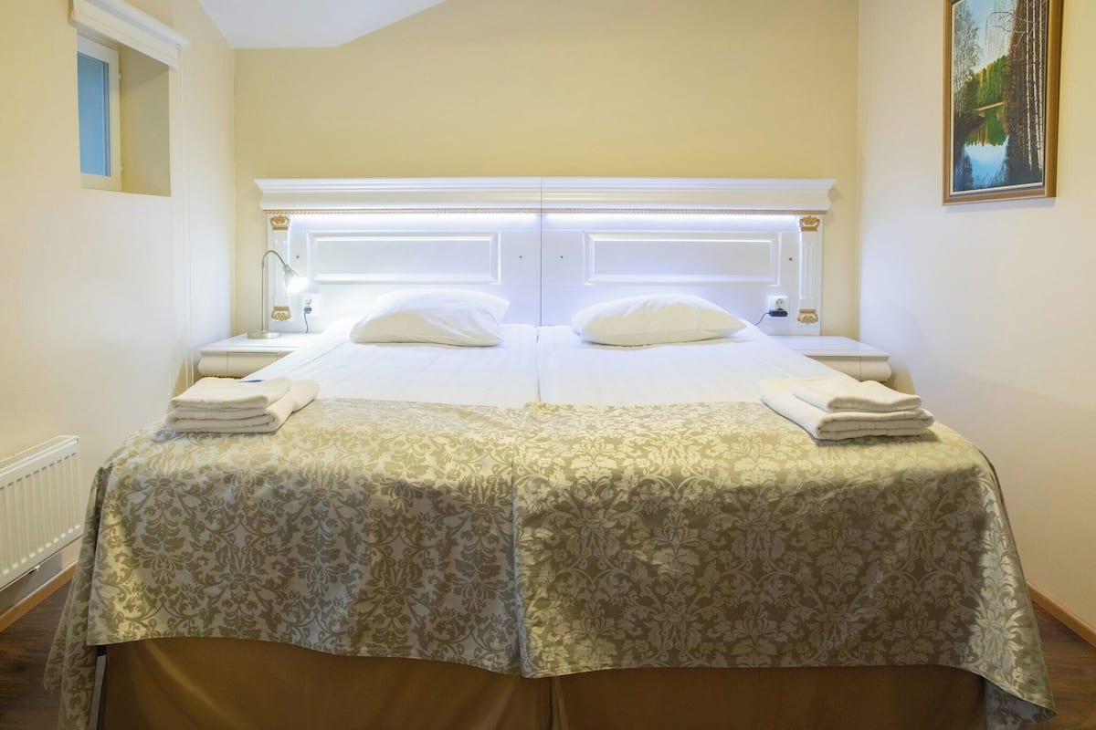 Cama de casal com colcha florida, duas almofadas e toalhas dobradas em ambos os lados.