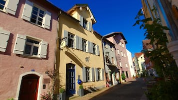 Uma rua de paralelepípedos estreita, ladeada por edifícios europeus tradicionais, com diversos estilos arquitetônicos e varandas.