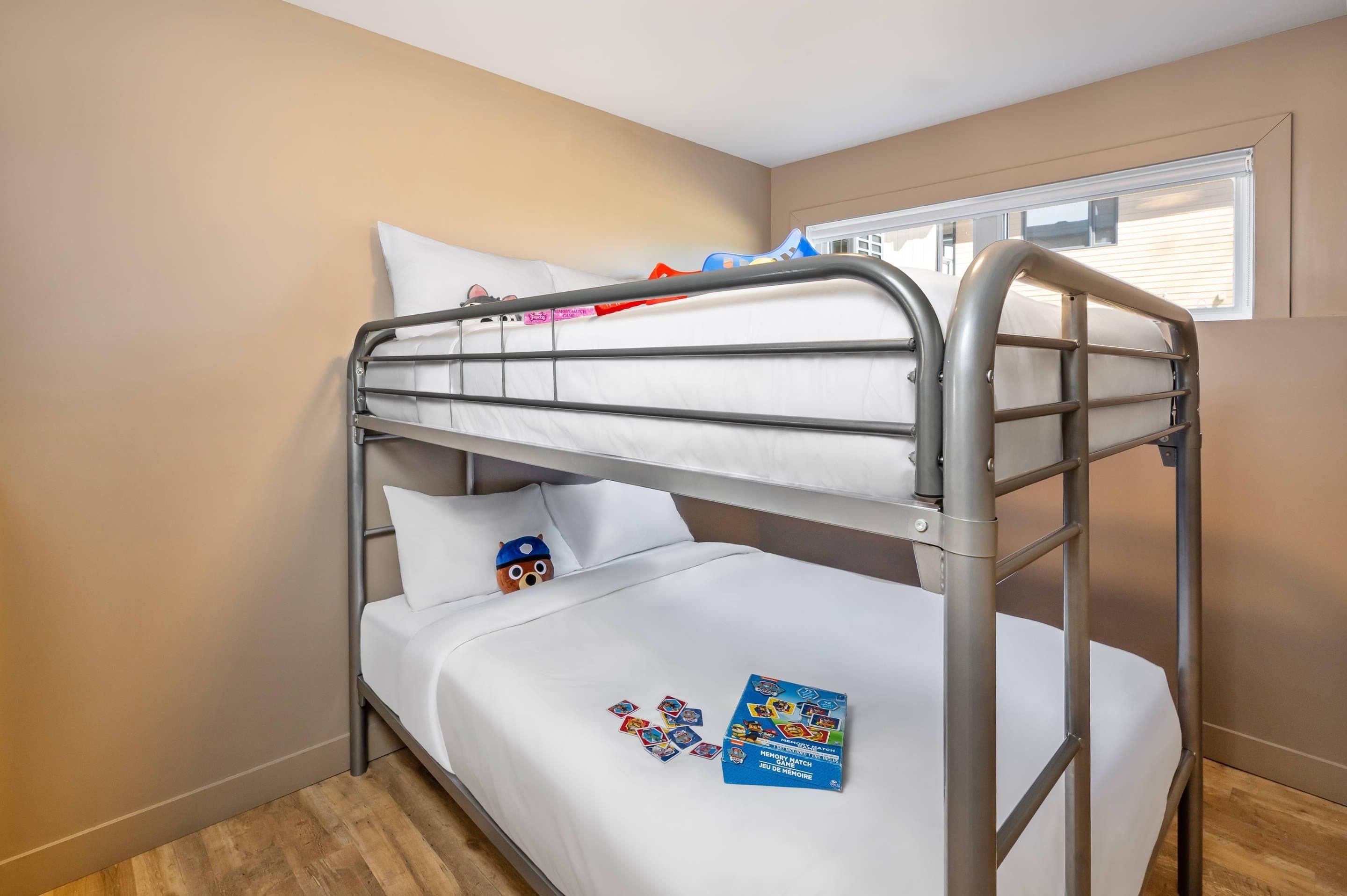 Uma cama beliche com estrutura de metal, roupa de cama branca e um brinquedo pequeno na cama de baixo.