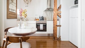 Uma cozinha com armários brancos, bancada de mármore, uma cadeira de madeira e um vaso com flores.