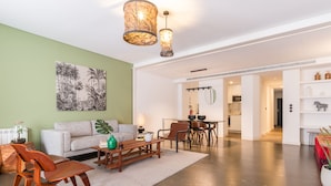 Uma sala de estar moderna com um sofá, cadeiras de madeira, uma mesa de centro e uma área de jantar com cadeiras e uma mesa.