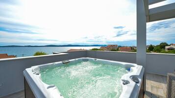 Uma banheira de hidromassagem numa varanda com vista para o mar e colinas ao longe.