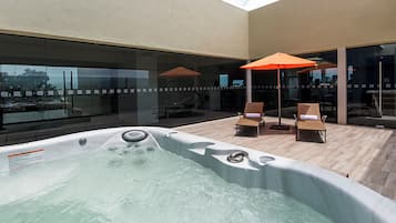 Terraço no telhado com banheira de hidromassagem, espreguiçadeiras e um guarda-sol laranja.