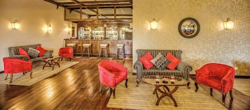 Uma área de bar com vigas de madeira, balcão e banquetas. Há duas sofás com almofadas vermelhas e pretas.