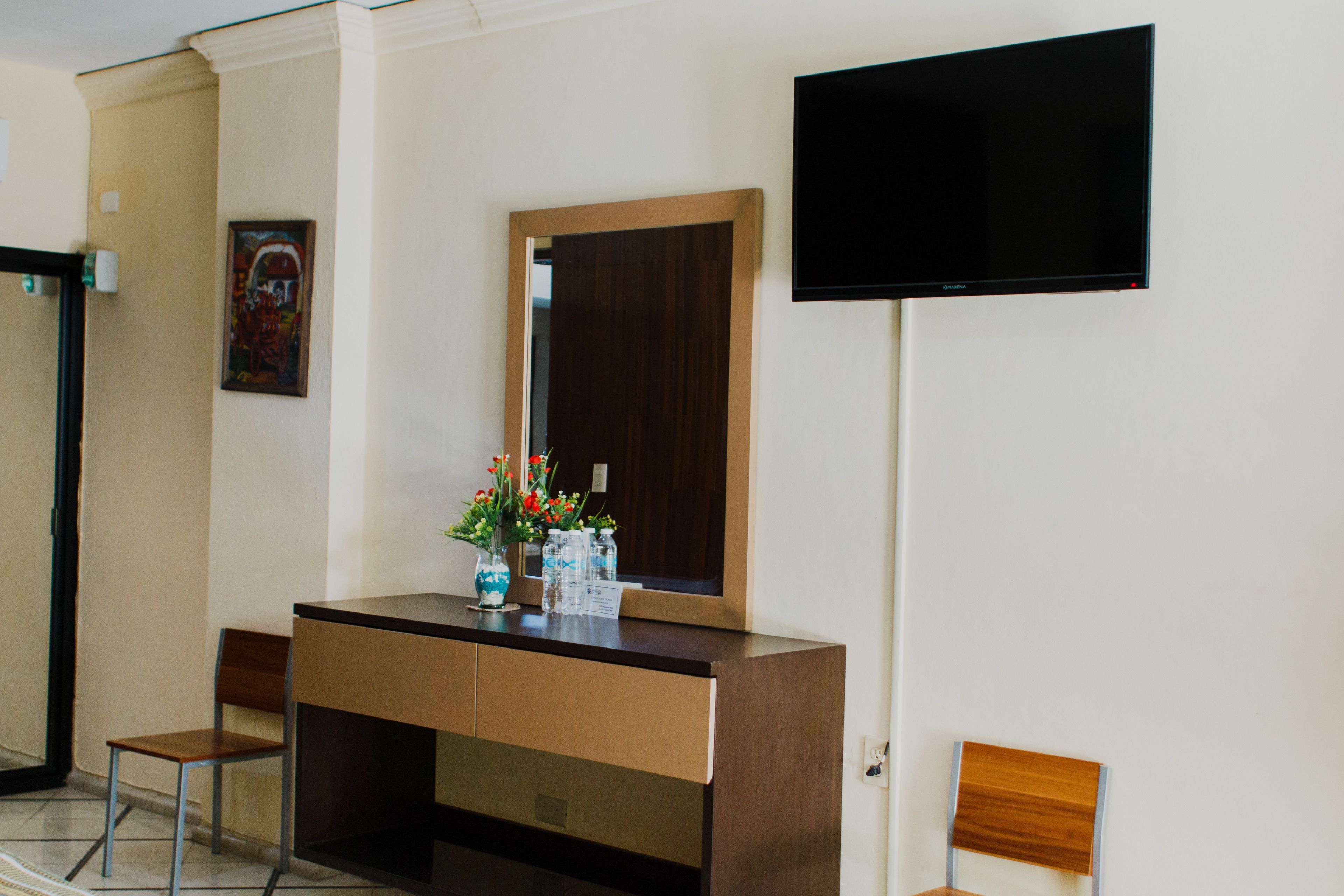 Quarto de hotel com penteadeira de madeira, televisão de tela plana, duas cadeiras e um espelho.