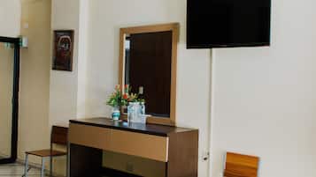 Quarto de hotel com penteadeira de madeira, televisão de tela plana, duas cadeiras e um espelho.