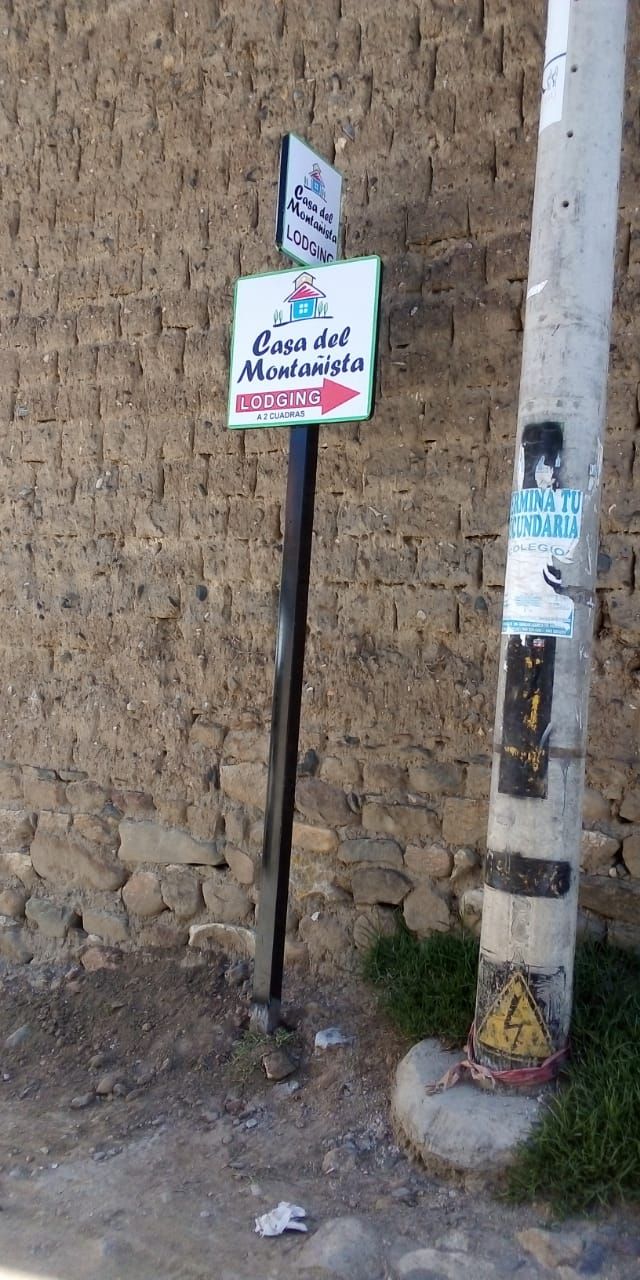 Placa de indicador com sinalização para o alojamento 'Casa del Montañista', uma parede de pedra e um poste com vários avisos.