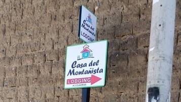 Placa de indicador com sinalização para o alojamento 'Casa del Montañista', uma parede de pedra e um poste com vários avisos.