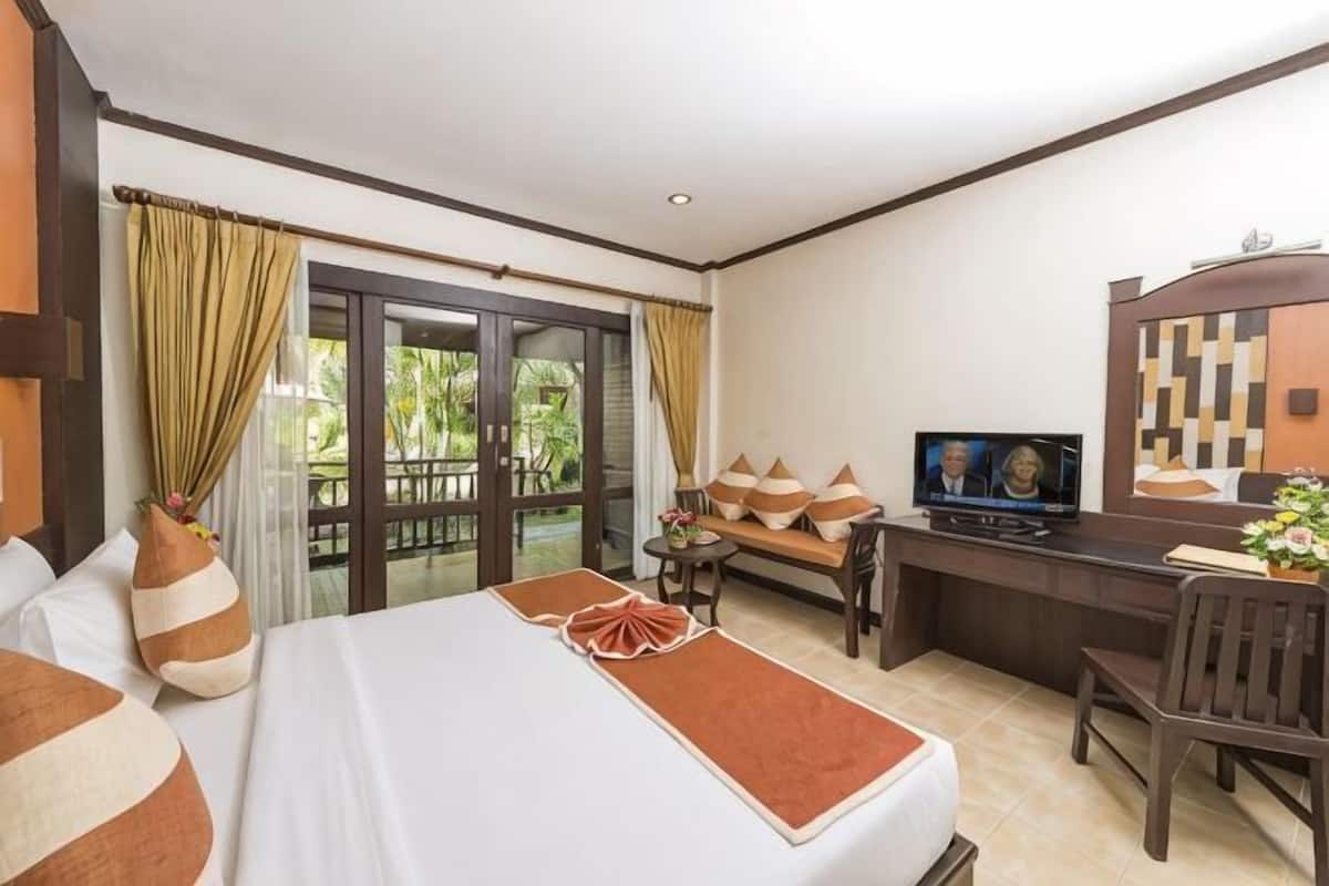 Quarto de hotel com uma cama, uma mesa, uma televisão e vista para o verde lá fora.