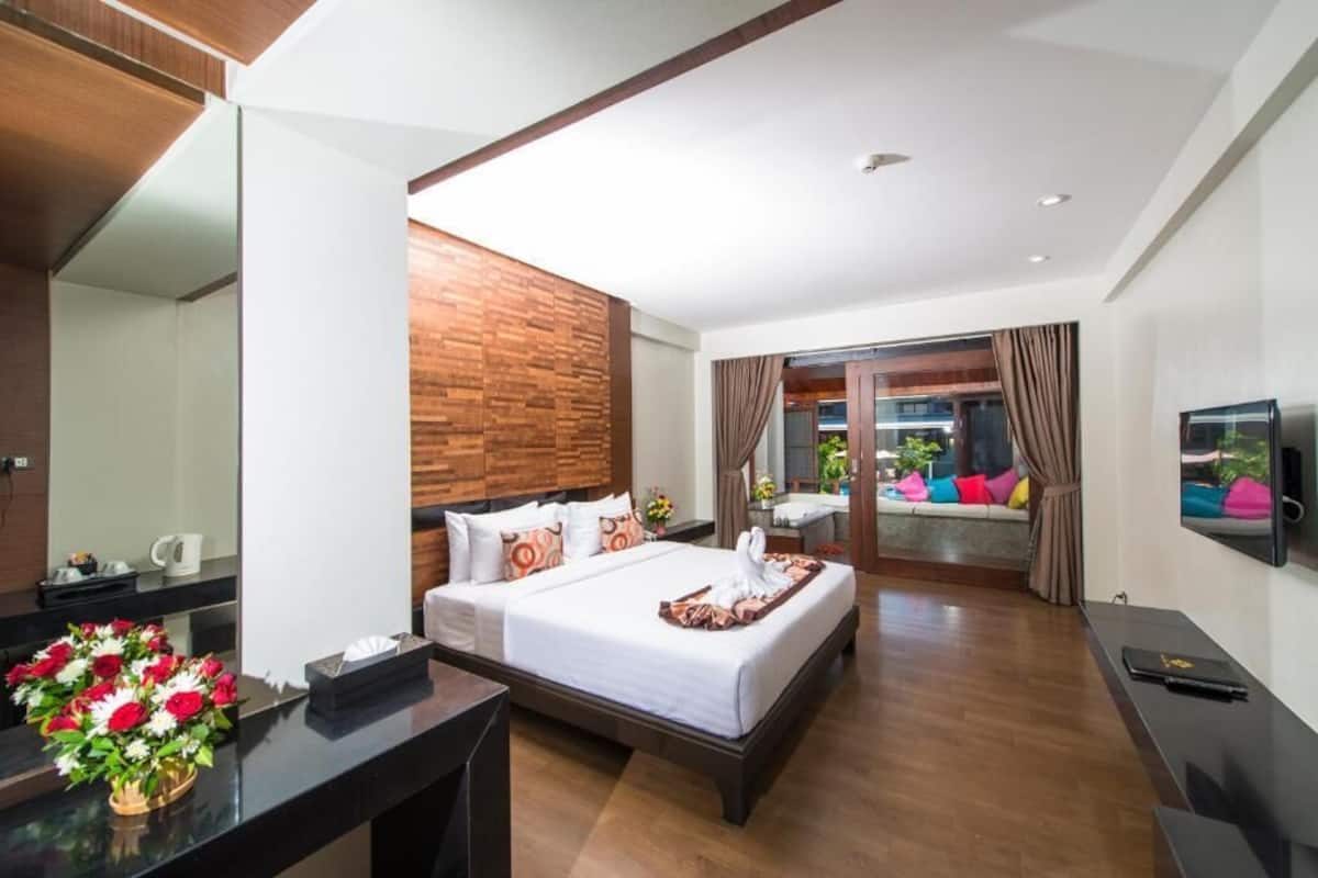 Quarto de hotel moderno com uma cama grande, uma escrivaninha com um vaso de flores, uma televisão e vista para a varanda.