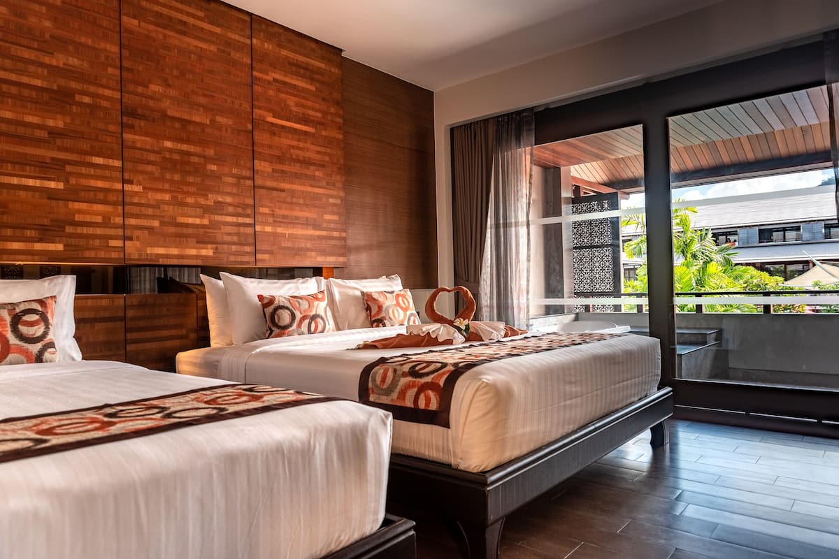 Quarto de hotel com duas camas, painéis de madeira nas paredes, uma janela grande com vista para áreas verdes e uma varanda.
