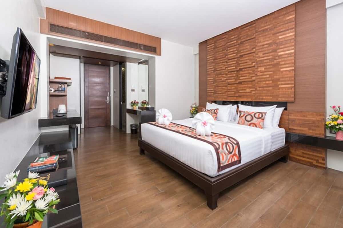 Quarto de hotel moderno com cama grande, cabeceira de madeira e televisão de tela plana na parede.