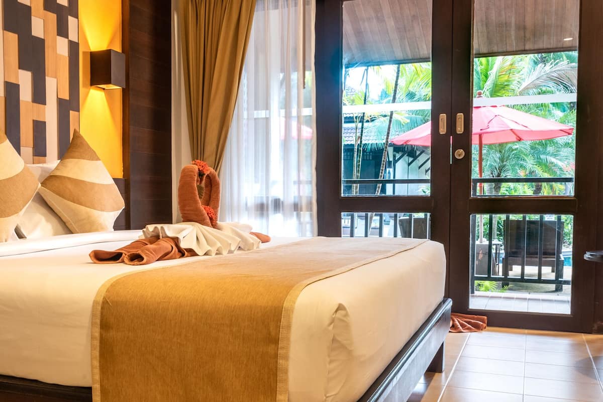Quarto de hotel com cama, cabeceira de madeira, janela grande com cortinas e vista para o exterior.