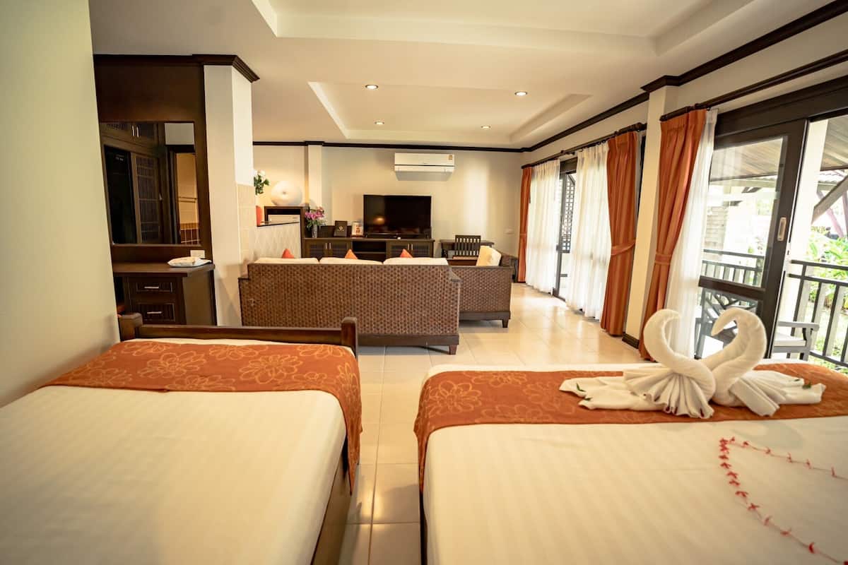 Quarto de hotel com duas camas, um sofá, uma televisão e varanda com cortinas.