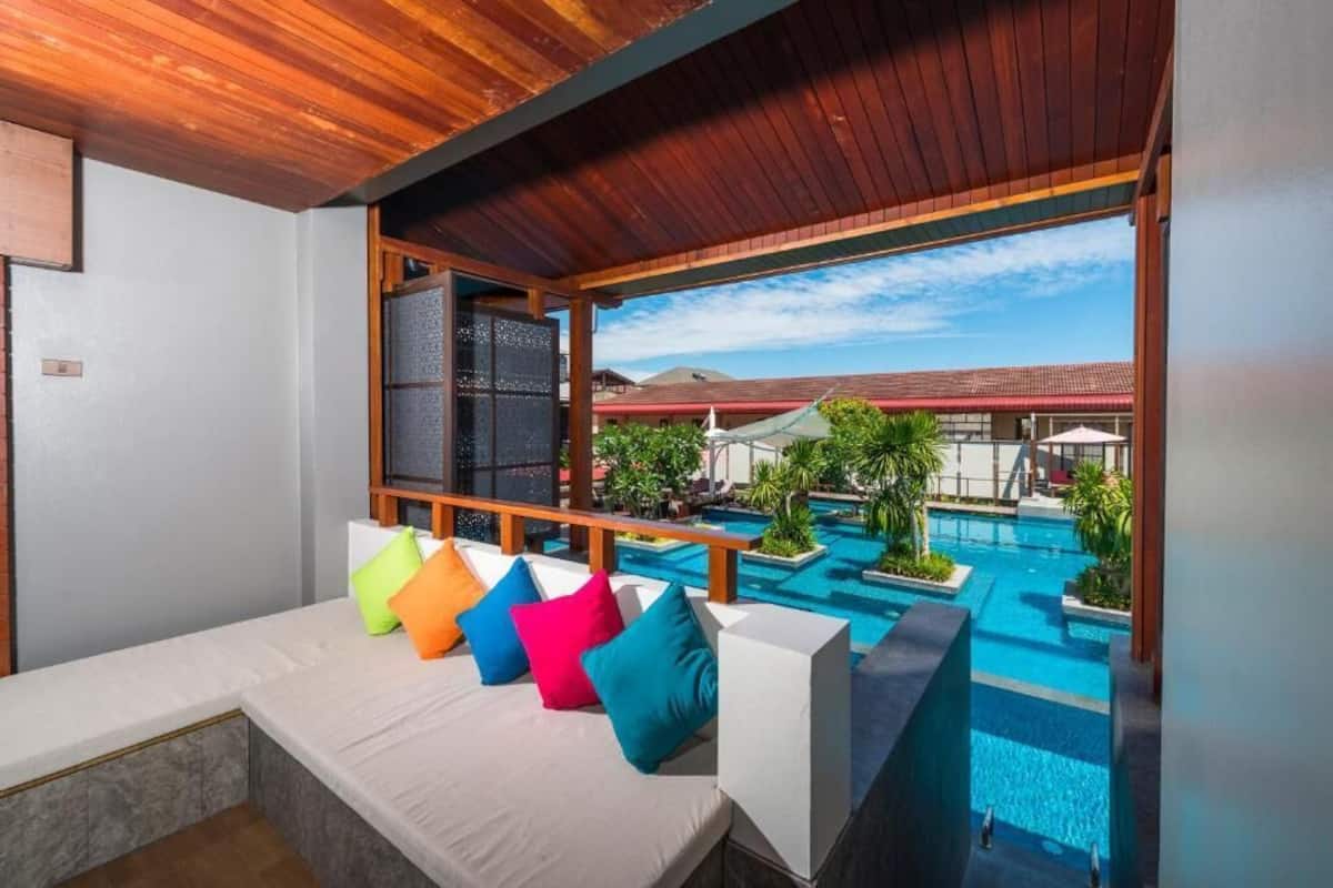 Quarto moderno com teto de madeira, vista para a piscina e almofadas coloridas.