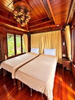 Quarto com duas camas, piso de madeira, luminária pendente e grandes janelas com cortinas.