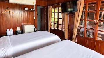 Quarto de hotel com duas camas, televisão, ventoinha no teto e janela com cortinas.