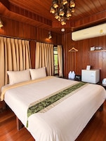 Quarto de hotel com cama grande, paredes de painel de madeira, luminária no teto, ar condicionado e mesa de cabeceira com rádio e uma xícara.