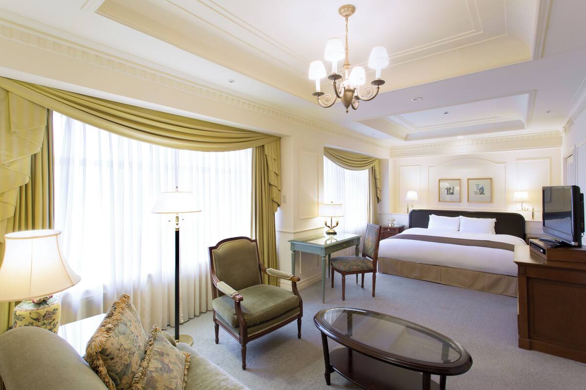 Quarto de hotel com cama, escrivaninha, cadeira, sofá e televisão.