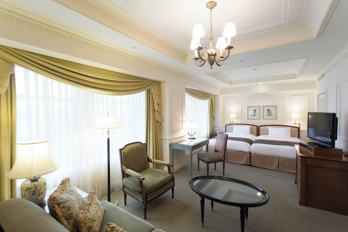 Quarto de hotel com cama, televisão, escrivaninha, cadeira e sofá.