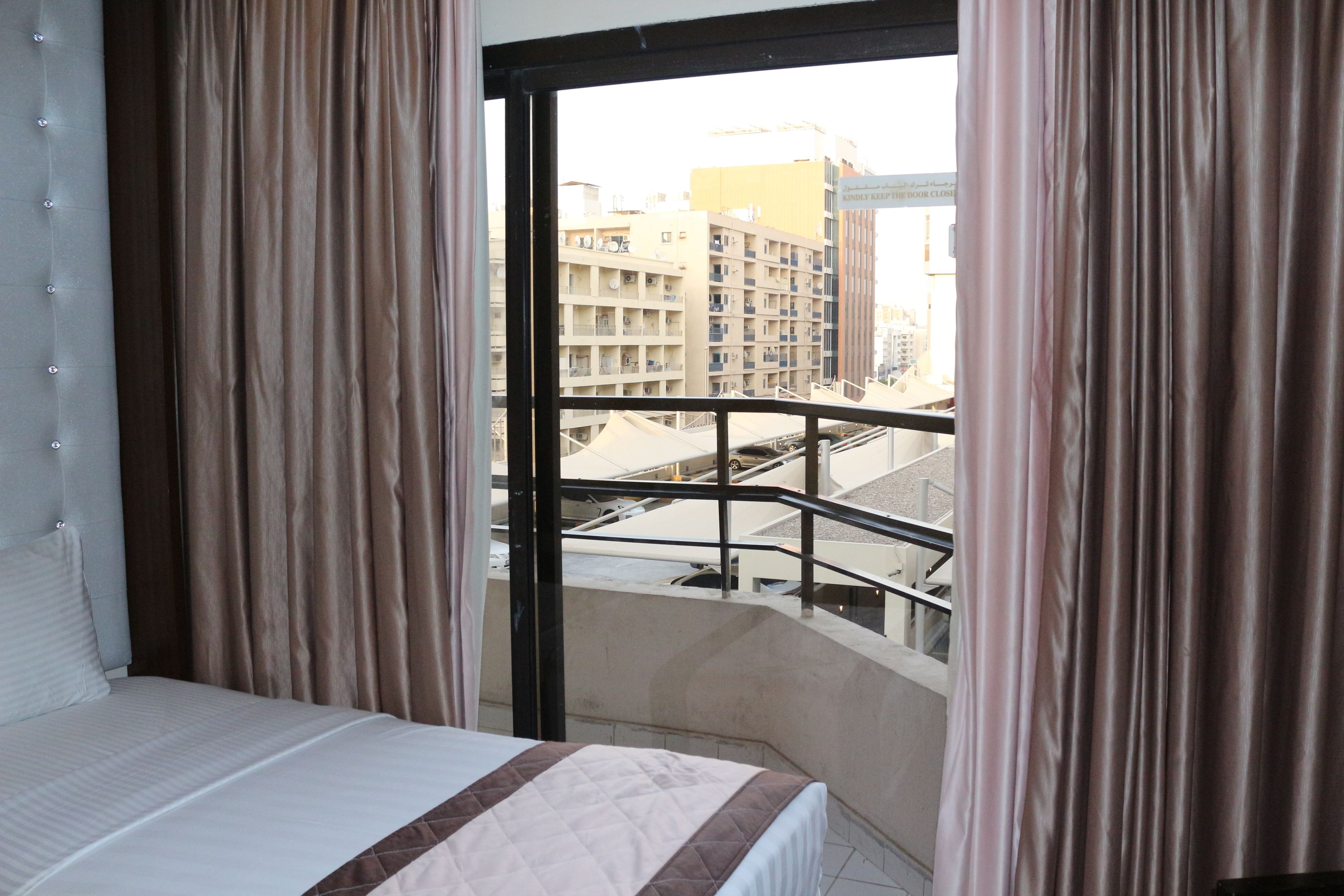 Quarto de hotel com cama, cortinas e varanda com vista para edifícios e uma grua de construção.