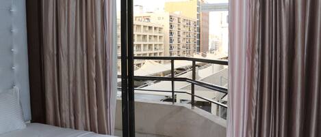 Quarto de hotel com cama, cortinas e varanda com vista para edifícios e uma grua de construção.