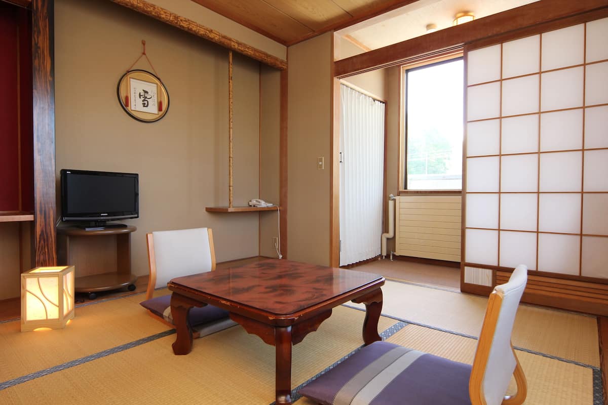 Um quarto japonês tradicional, com piso de tatame, uma mesa de madeira baixa, uma televisão e portas deslizantes shoji.