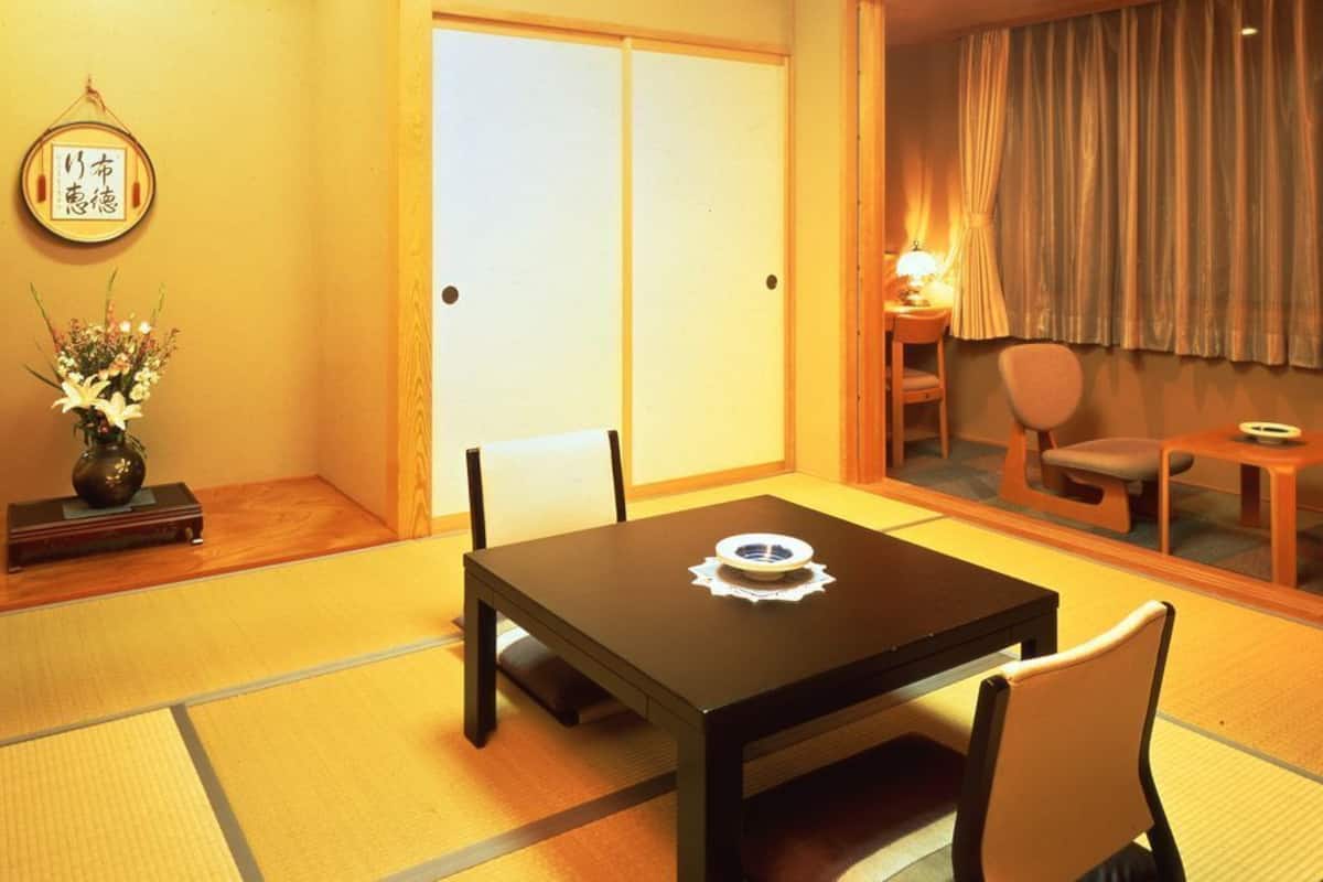 Um quarto japonês tradicional com tatames, uma mesa baixa com um prato decorativo, uma cadeira e uma porta deslizante.