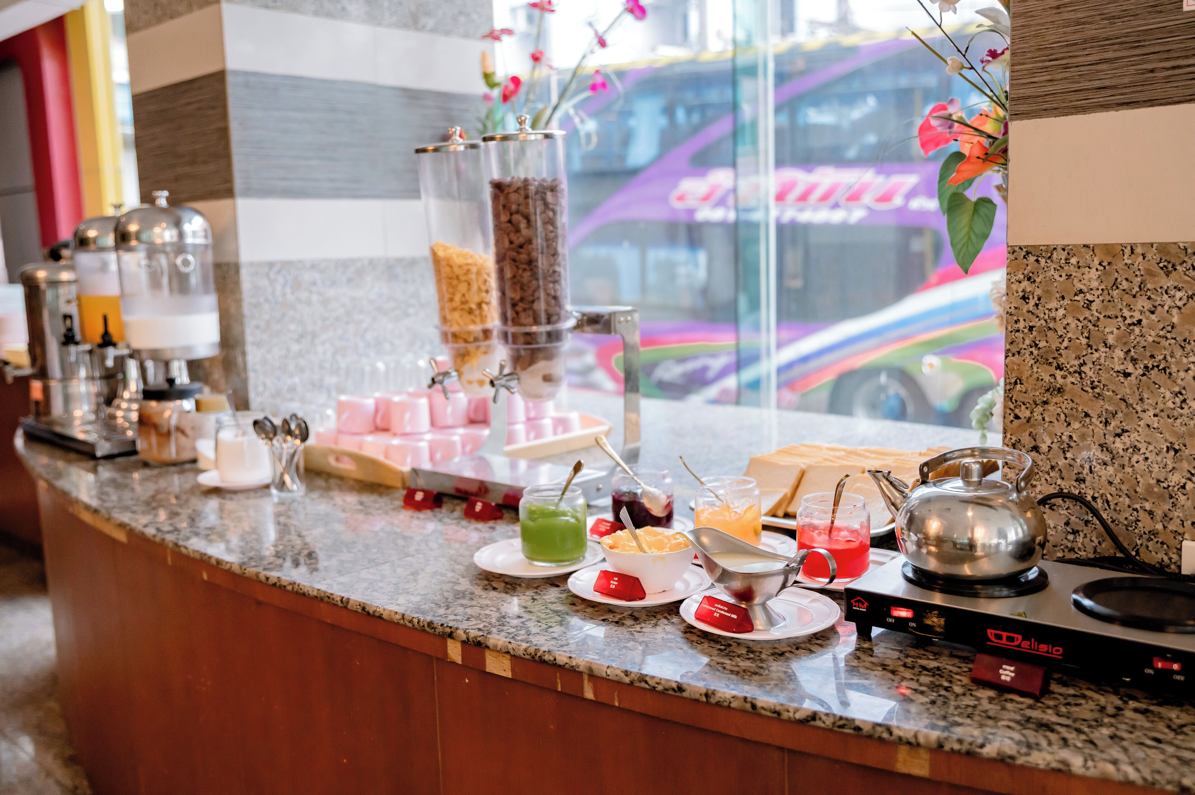 Balcão de recepção de hotel com diversos serviços, incluindo uma máquina de café, chaleira e exposição de bebidas coloridas.