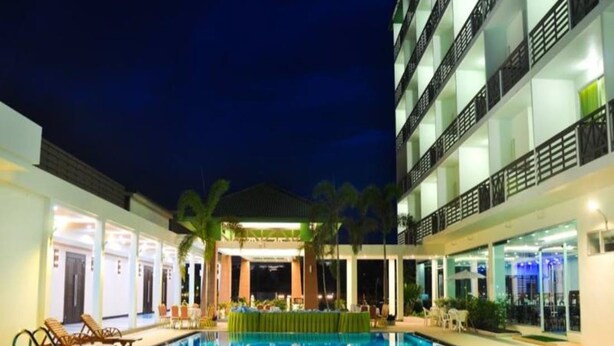 Piscina com espreguiçadeiras e área coberta, cercada por edifícios com varandas e mesas externas.