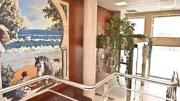 Um saguão de hotel com um mural de uma cena de praia, uma escada e plantas de interior.