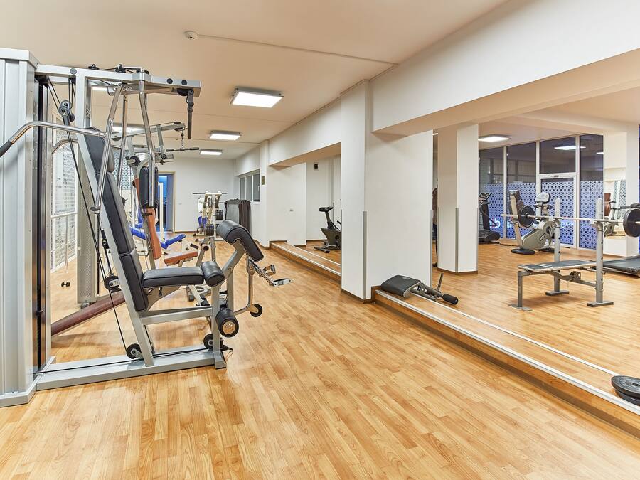 Uma academia com piso de madeira, equipamentos de exercícios e espelhos.