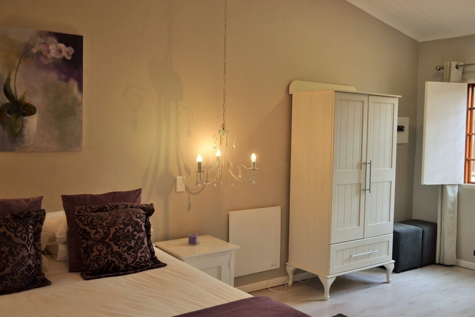 Quarto com cama, mesas de cabeceira, guarda-roupa, radiador e janela com cortinas.