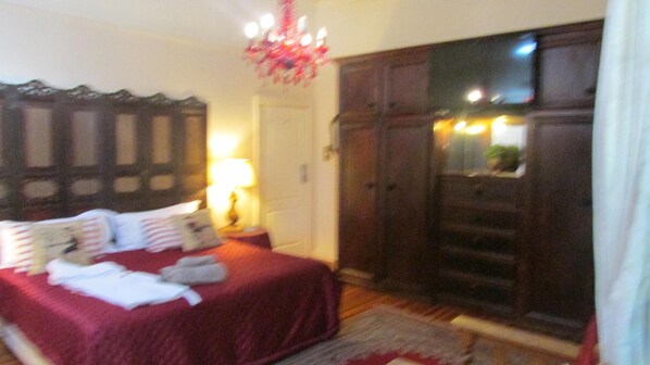 Quarto com cama grande, guarda-roupa e mesa de cabeceira com abajur.