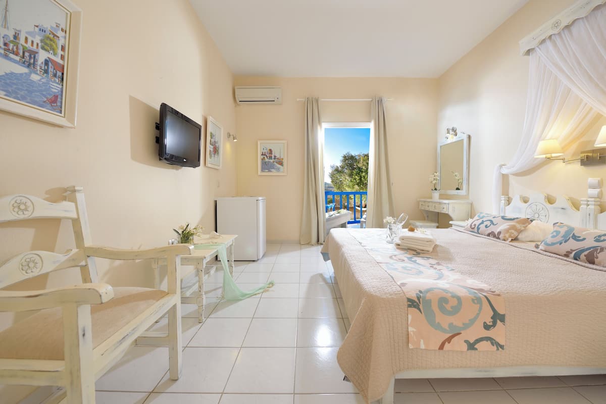 Quarto de hotel com cama, escrivaninha, cadeira, televisão e varanda com vista.