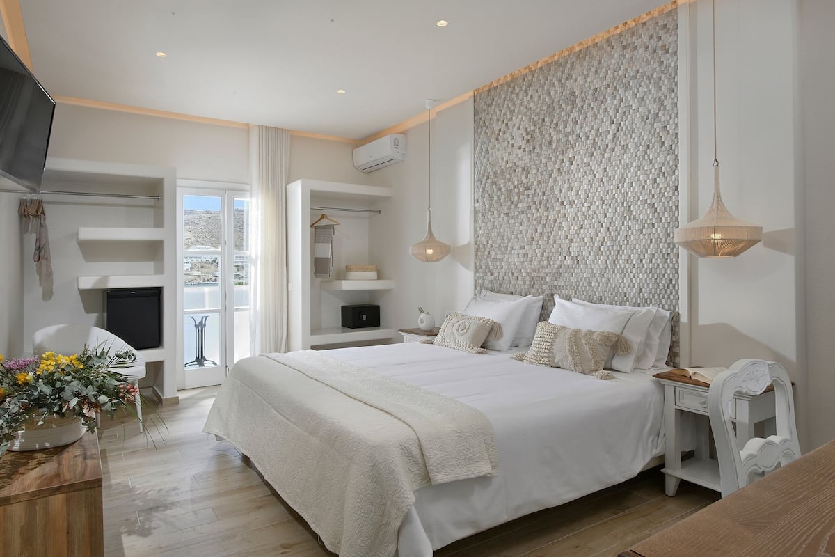 Quarto moderno com uma cama grande, mesas de cabeceira, televisão e vista para o exterior.