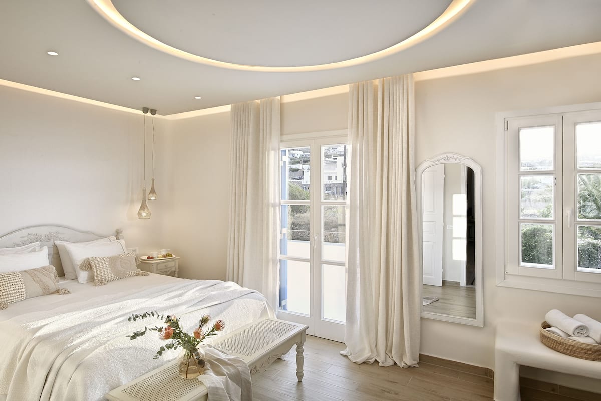 Quarto com cama grande, mesas de cabeceira, espelho e janela com cortinas.