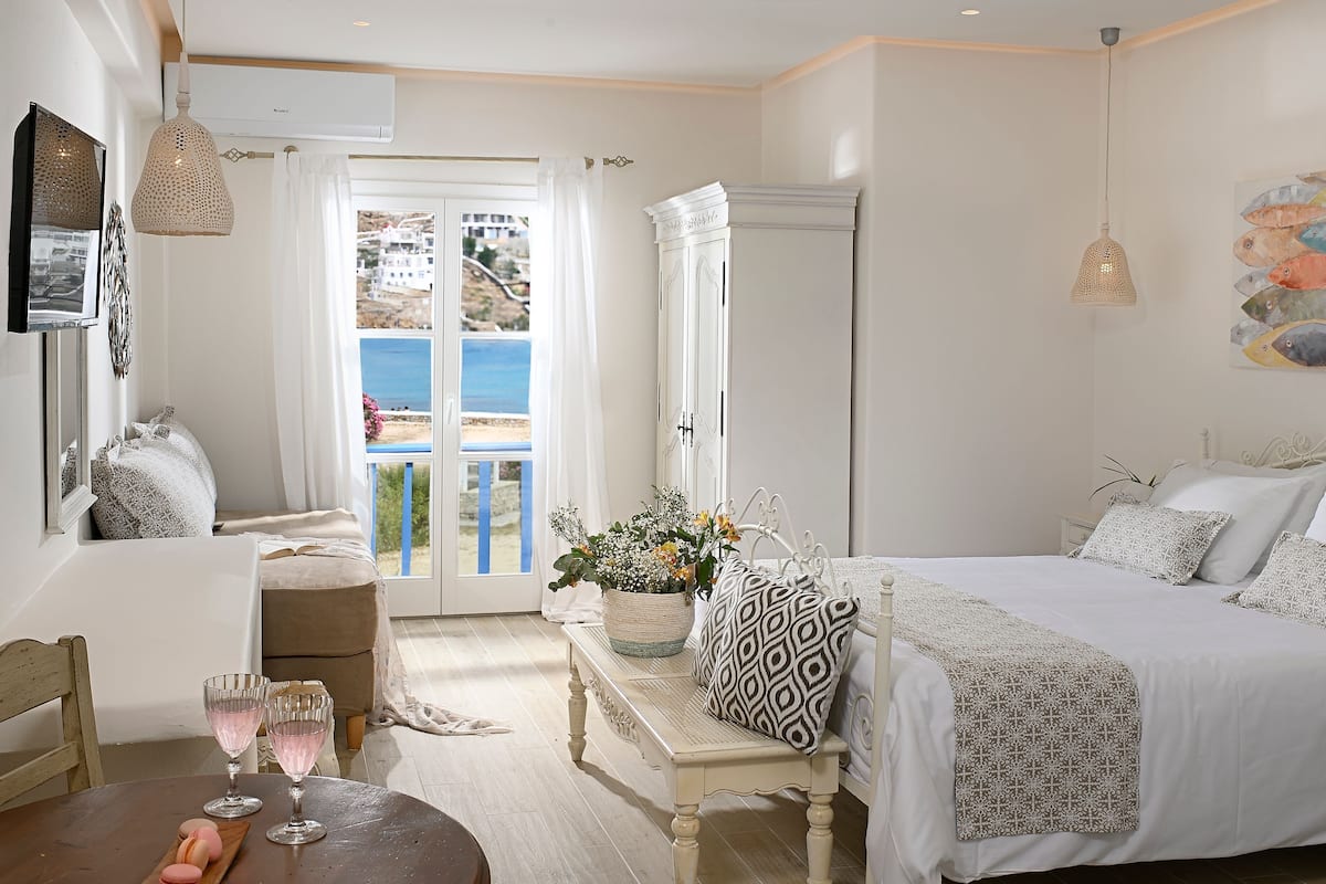 Quarto com cama, mesa de cabeceira e vista para o mar através de uma porta de vidro.