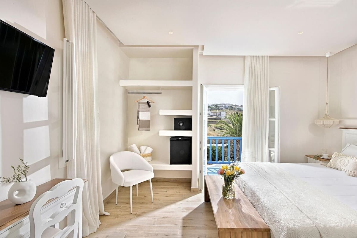 Quarto moderno com cama, escrivaninha, cadeira, televisão e varanda com vista.