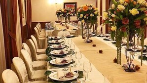 Uma longa mesa de jantar com pratos, copos e talheres dispostos com cuidado, ladeada por cadeiras e decorada com arranjos florais.
