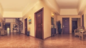 Um corredor amplo com escada de madeira, uma porta grande de madeira e um espaço de estar com cadeiras de vime e um vaso.